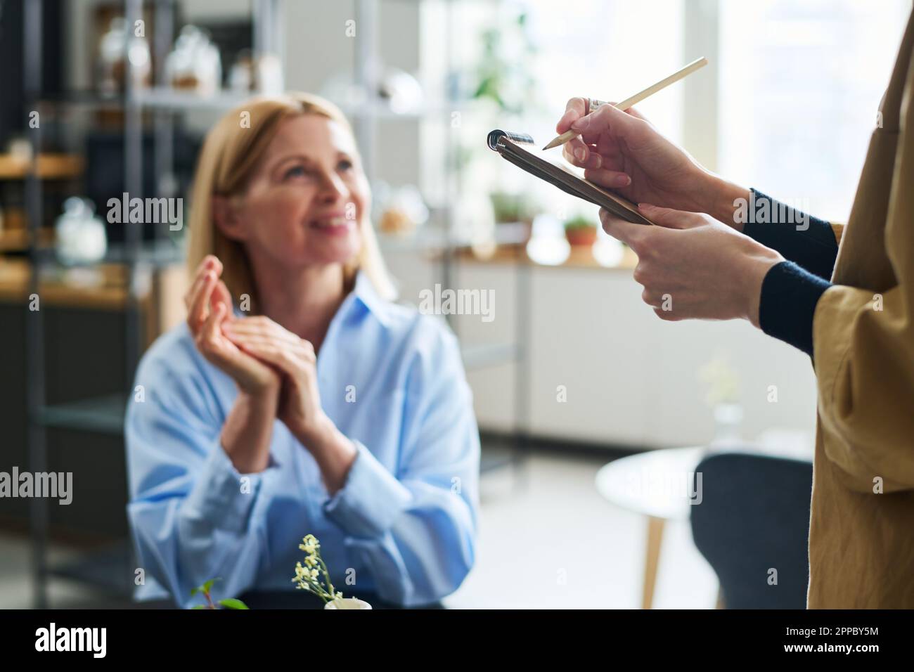 Hands of young waitress or cafe clerk with pen making notes in notepad ...
