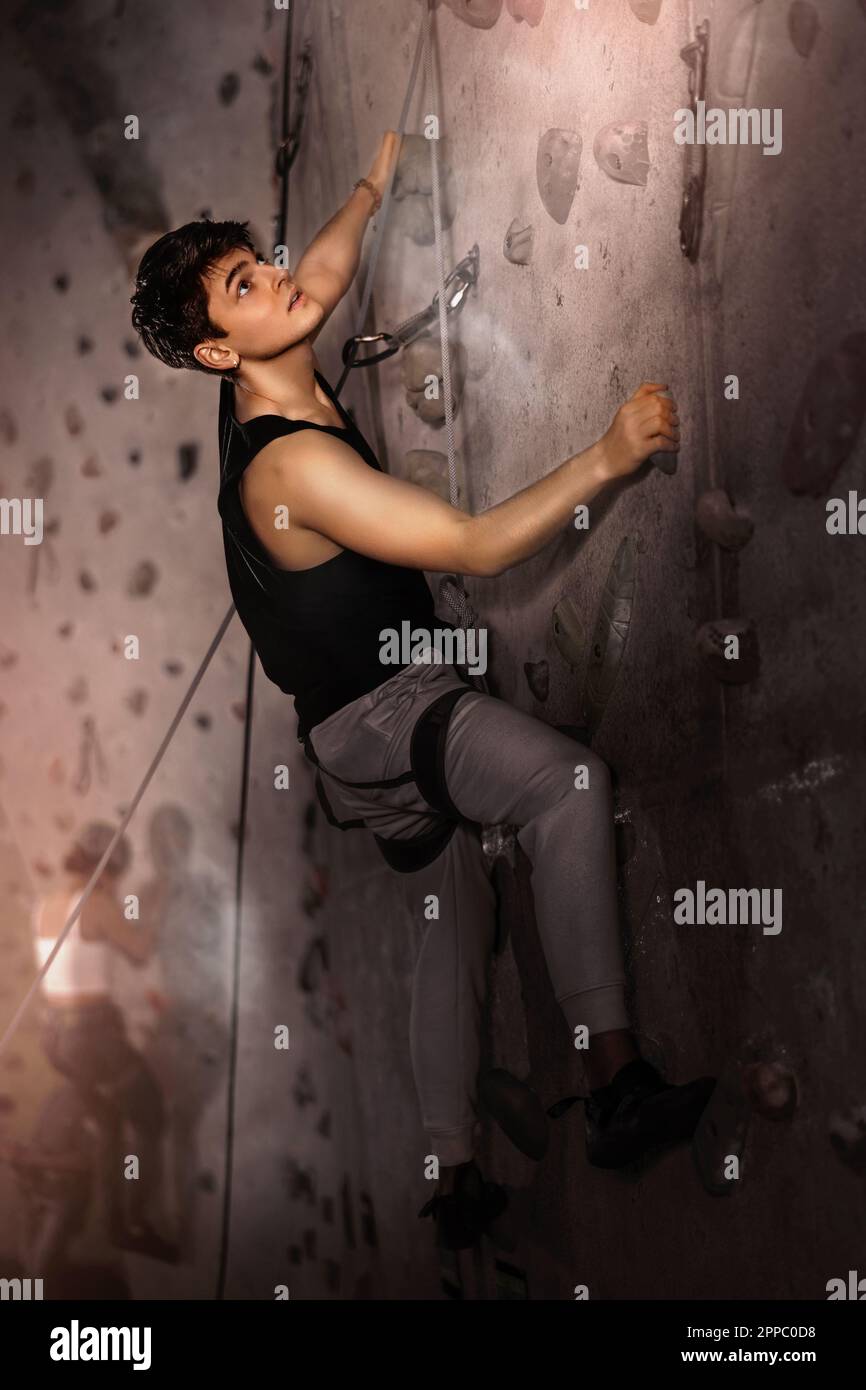 Side view of sportive young male climber moving up, using safety top ...