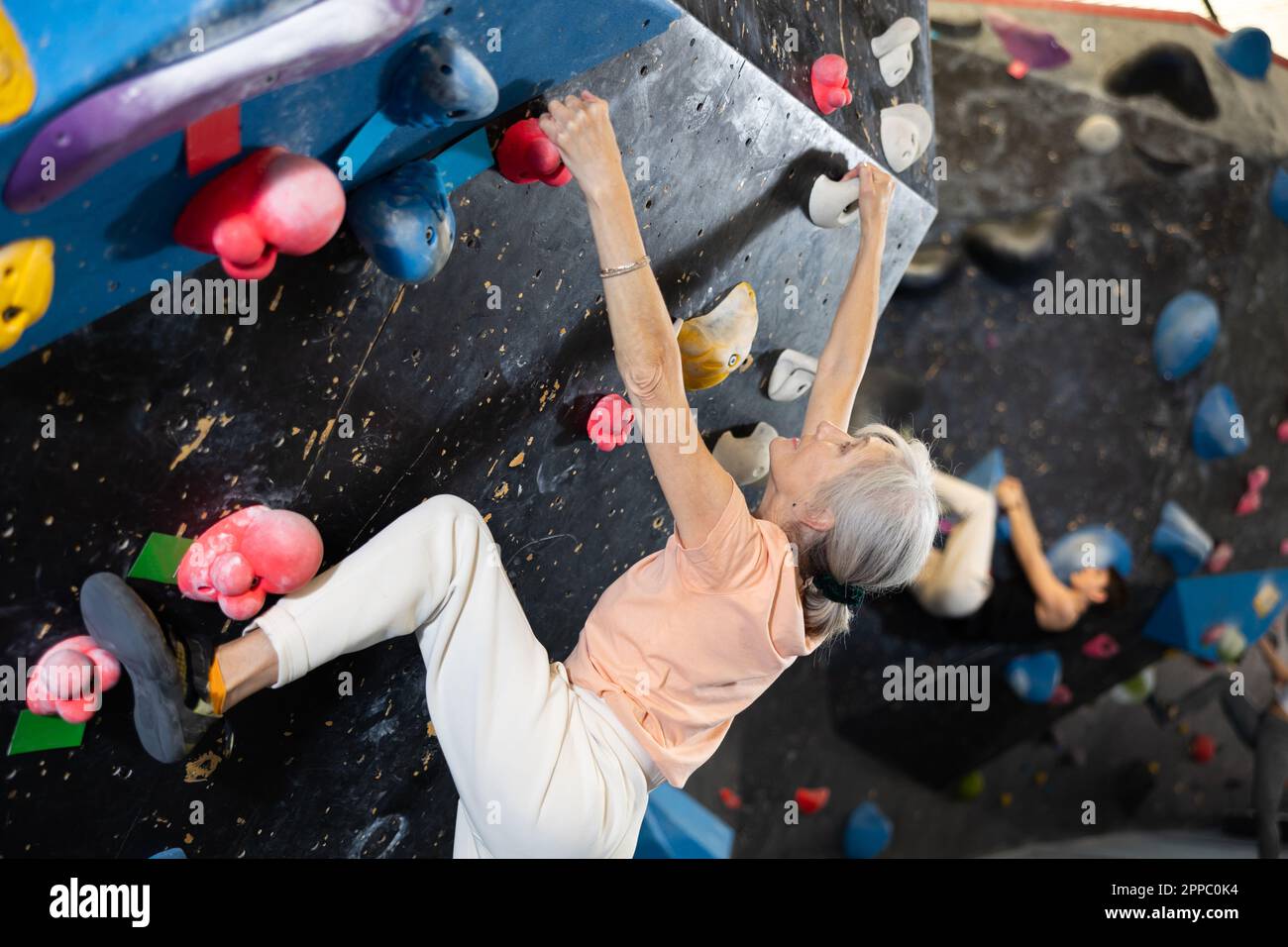 Mature female fitness climber training at bouldering gym.Woman rise up ...