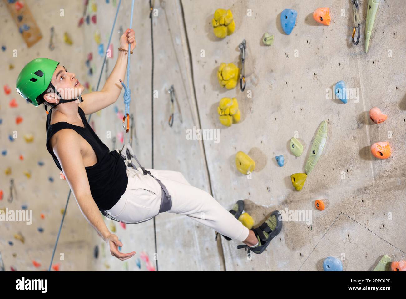 Well-equipped, positive young man going down on rope after reaching top ...