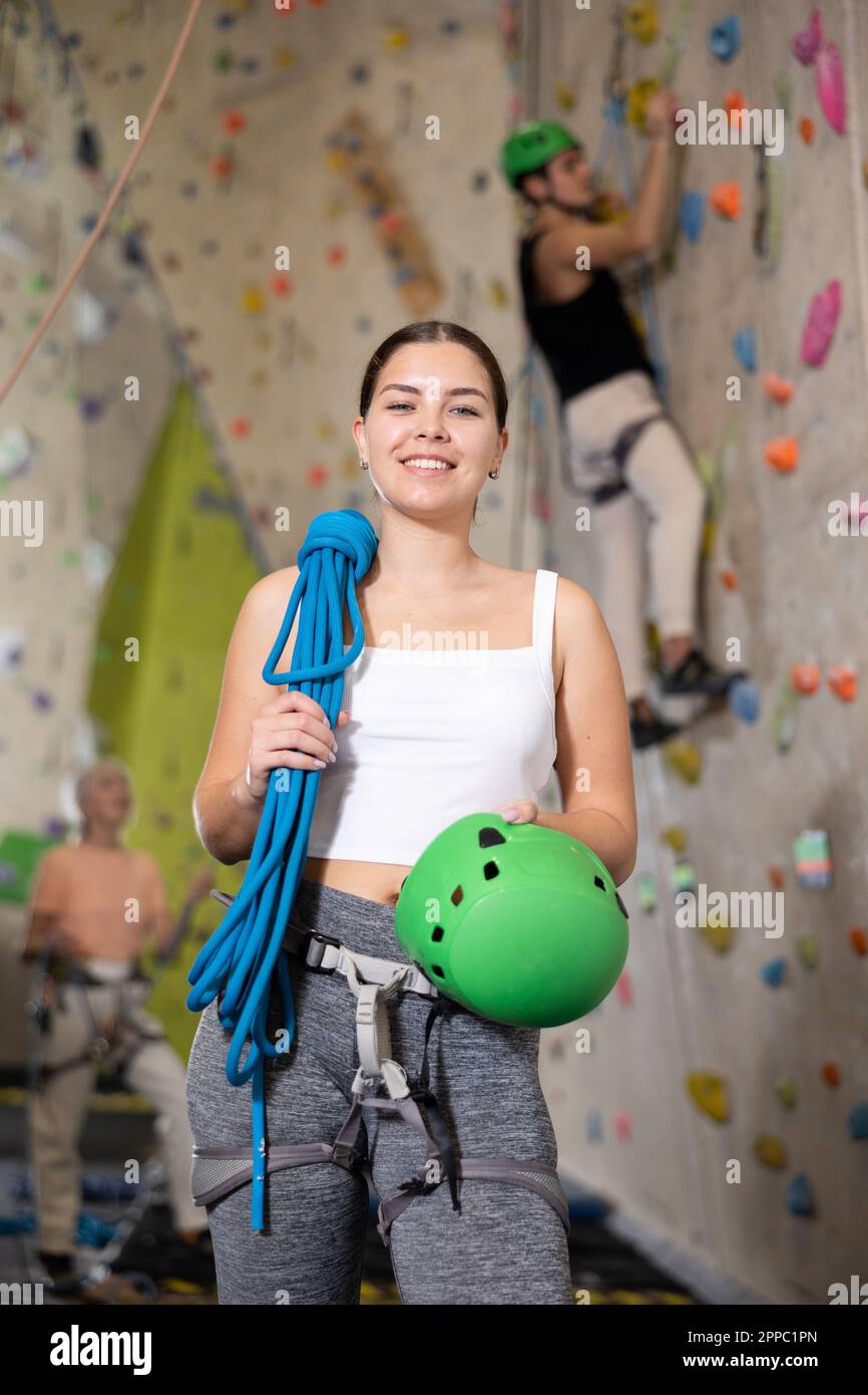 Smiling active young woman standing with rope on shoulders and helmet ...