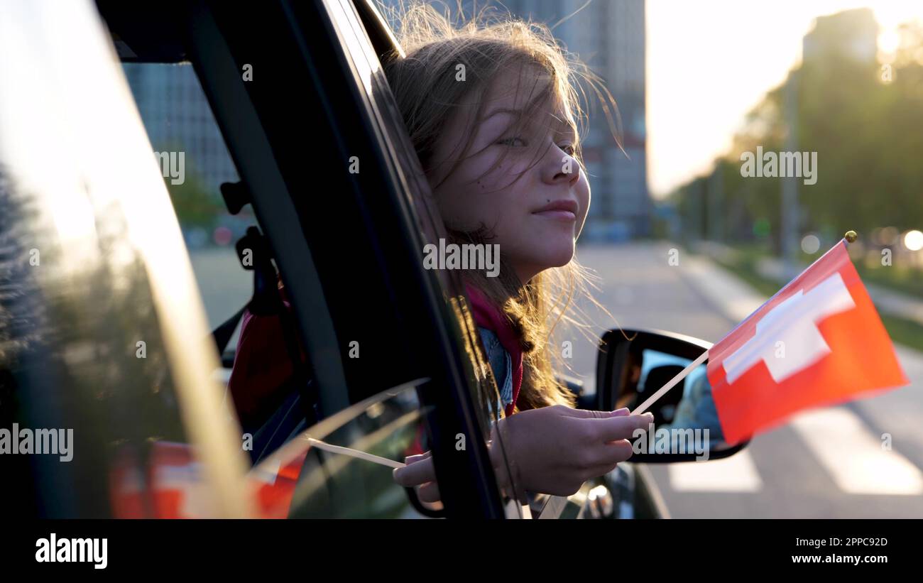 Side view of little pretty girl in good mood showing Swiss flag out of ...