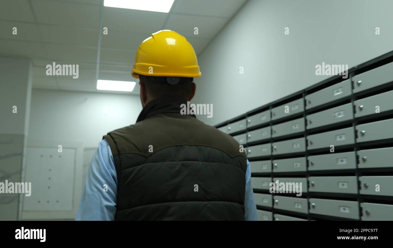 Back view of male worker in yellow helmet walking indoor in residential ...