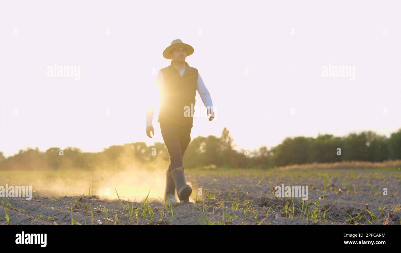 Joyful handsome male farmer walks in rubber boots on land through small ...