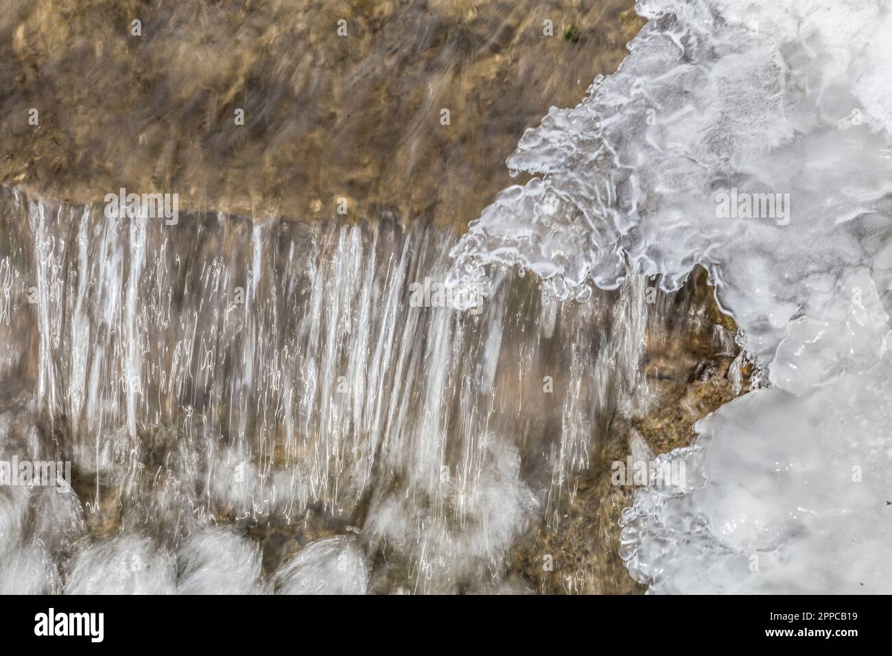 A scenic view of a small waterfall cascading over rugged rocks, covered ...