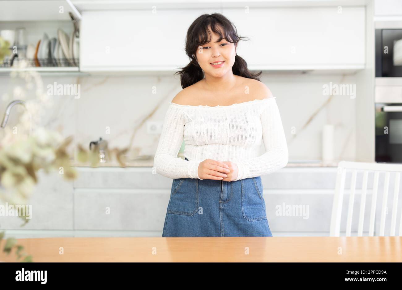 Portrait of young housewife in white blouse and denim skirt standing in ...