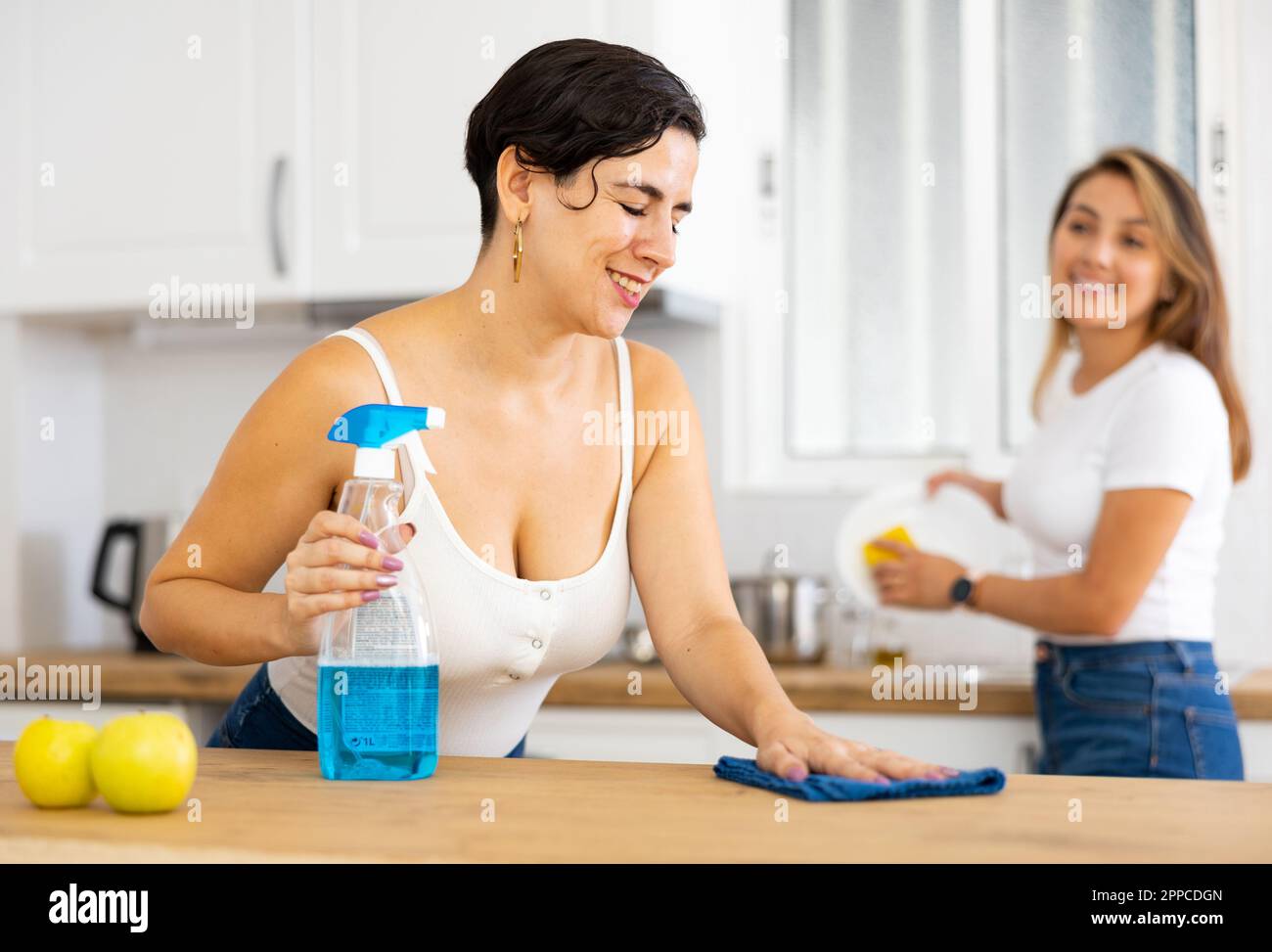 Positive young Latina cleaning home kitchen with sister Stock Photo - Alamy