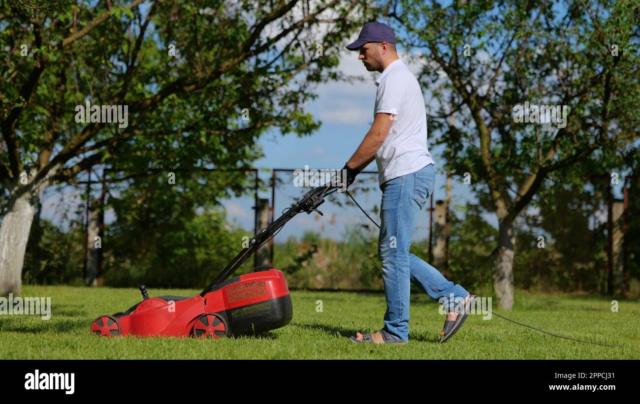 Side view of handsome male worker working in private garden mowing lawn ...
