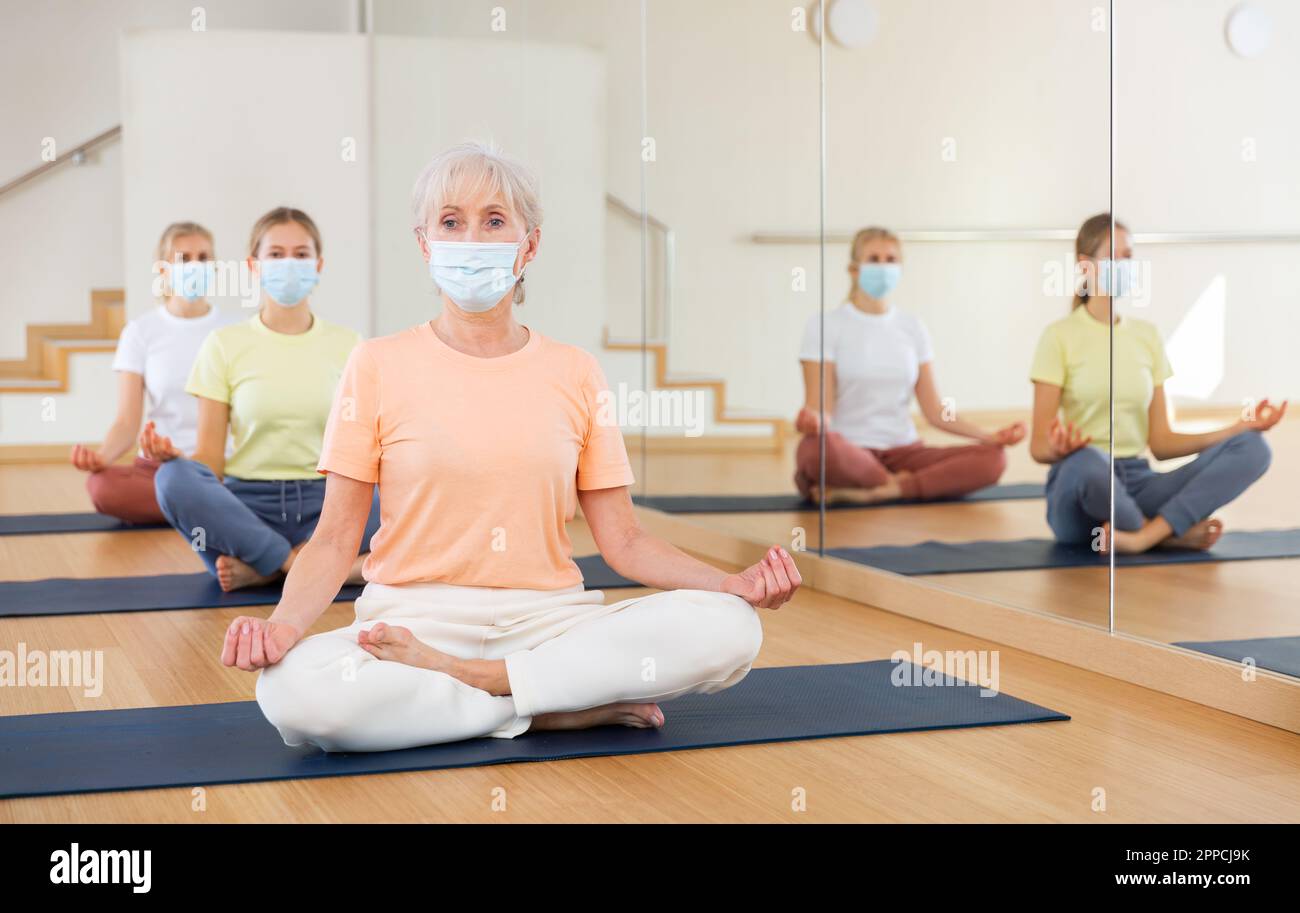 Group of people in protective mask sitting in lotus position practicing ...