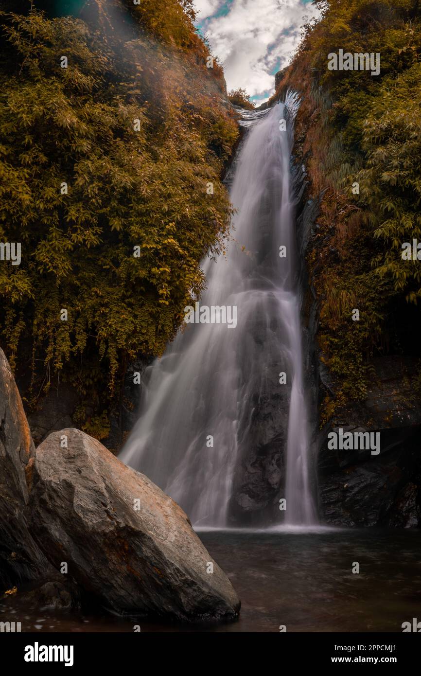 A vertical image of a small waterfall cascading into a river surrounded ...