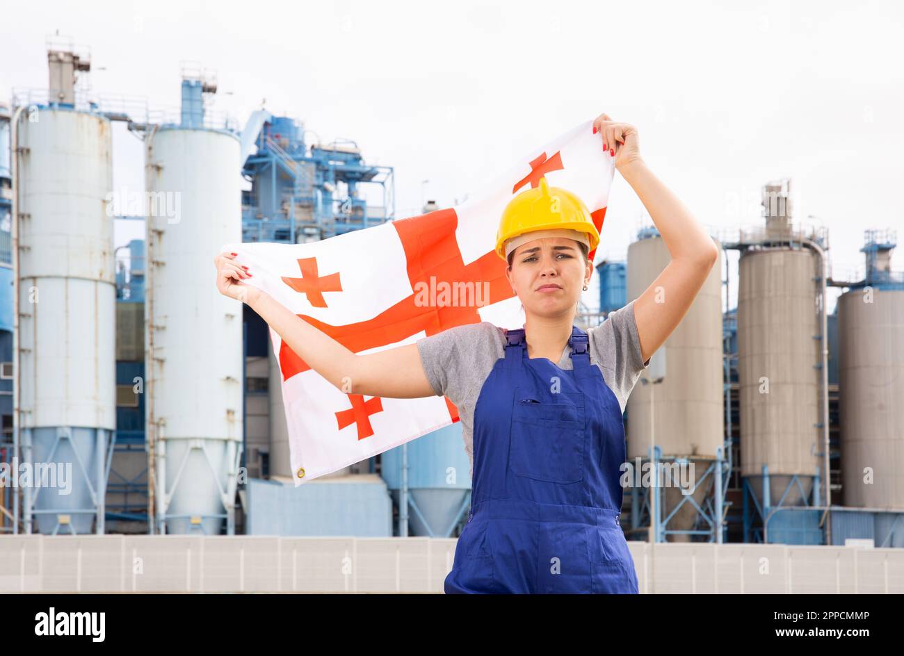 Upset disappointed young female engineer in helmet waving state flag of ...