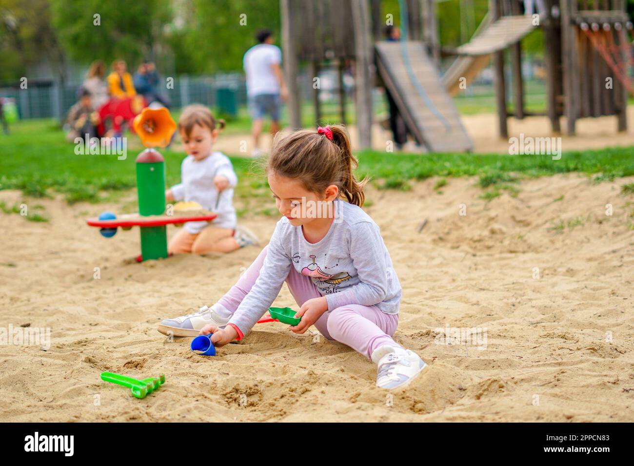 Kids playing at park - Little girls sitting down in sand playing ...