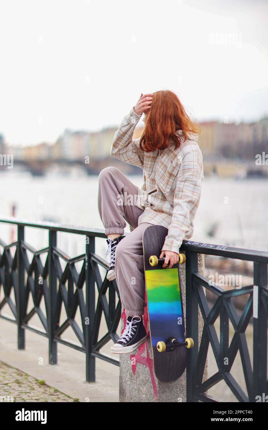 teen girl touch her red hair sitting on the curb and hold her ...