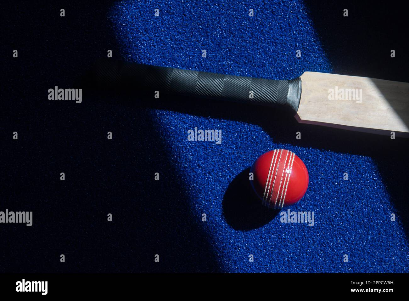 Cricket bat and red ball with natural lighting on blue background ...