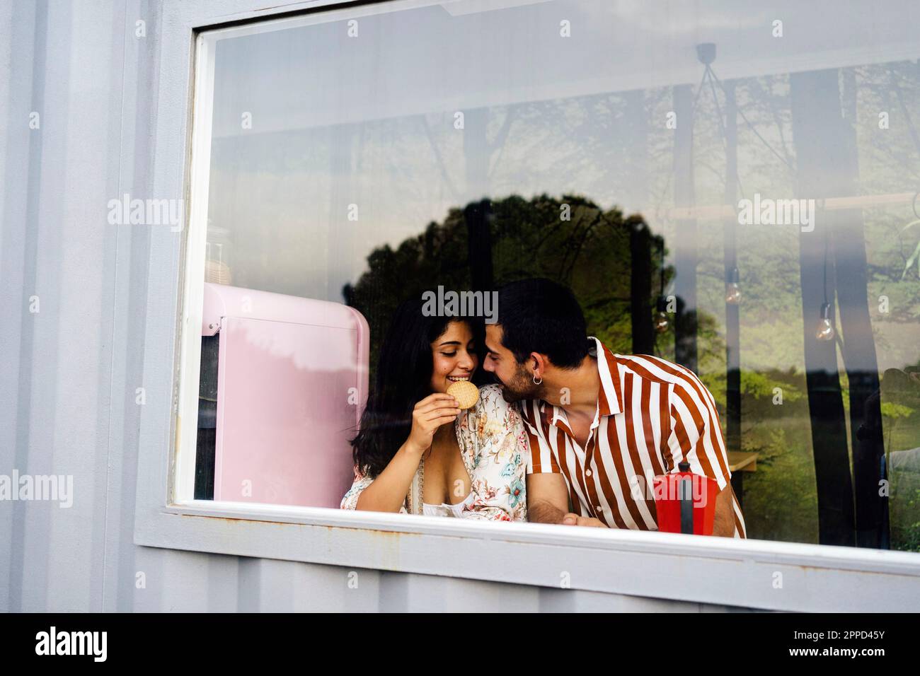 Romantic couple enjoying snacks in kitchen seen through window of ...