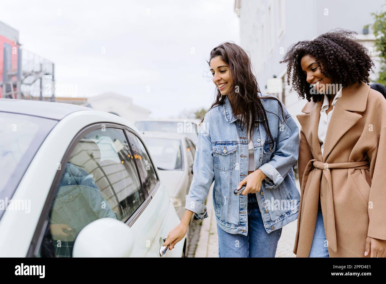 Smiling young woman with friend unlocking car with remote key Stock ...