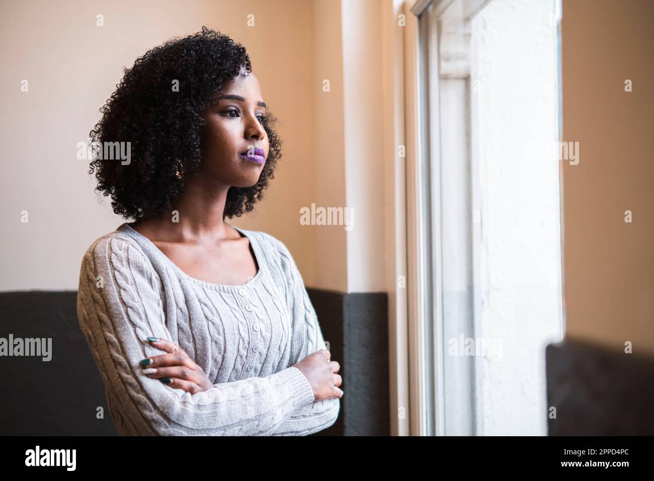 Woman with arms crossed looking out of window Stock Photo - Alamy