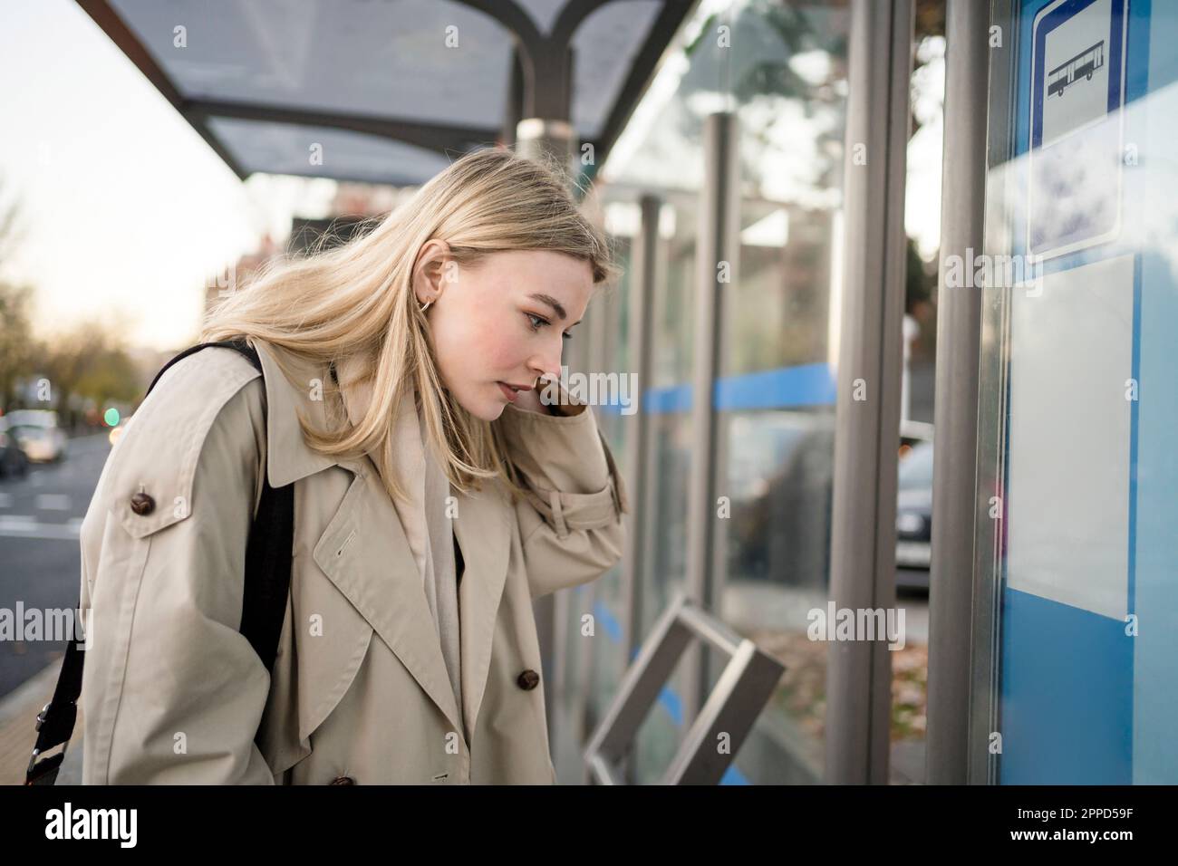 Blond young woman checking bus schedule at station Stock Photo - Alamy
