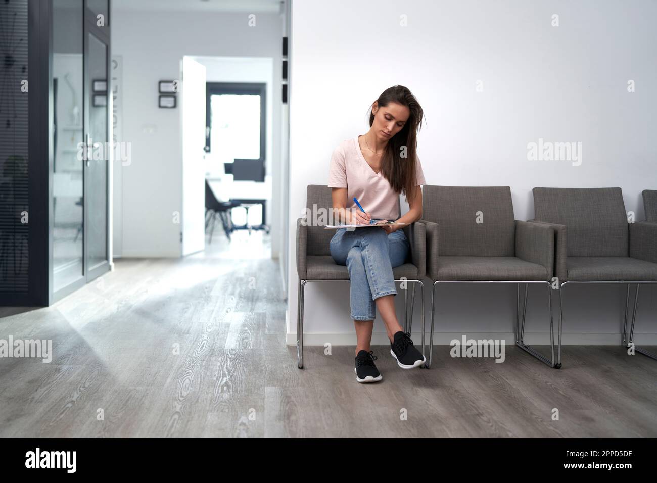 Woman filling form sitting on chair in waiting room Stock Photo - Alamy