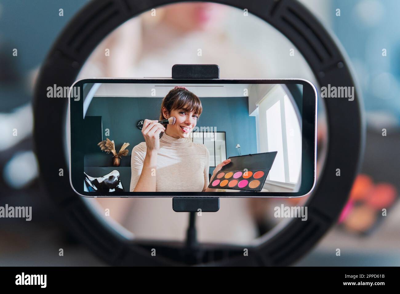 Smart phone screen mounted on ring light with vlogger filming make-up ...
