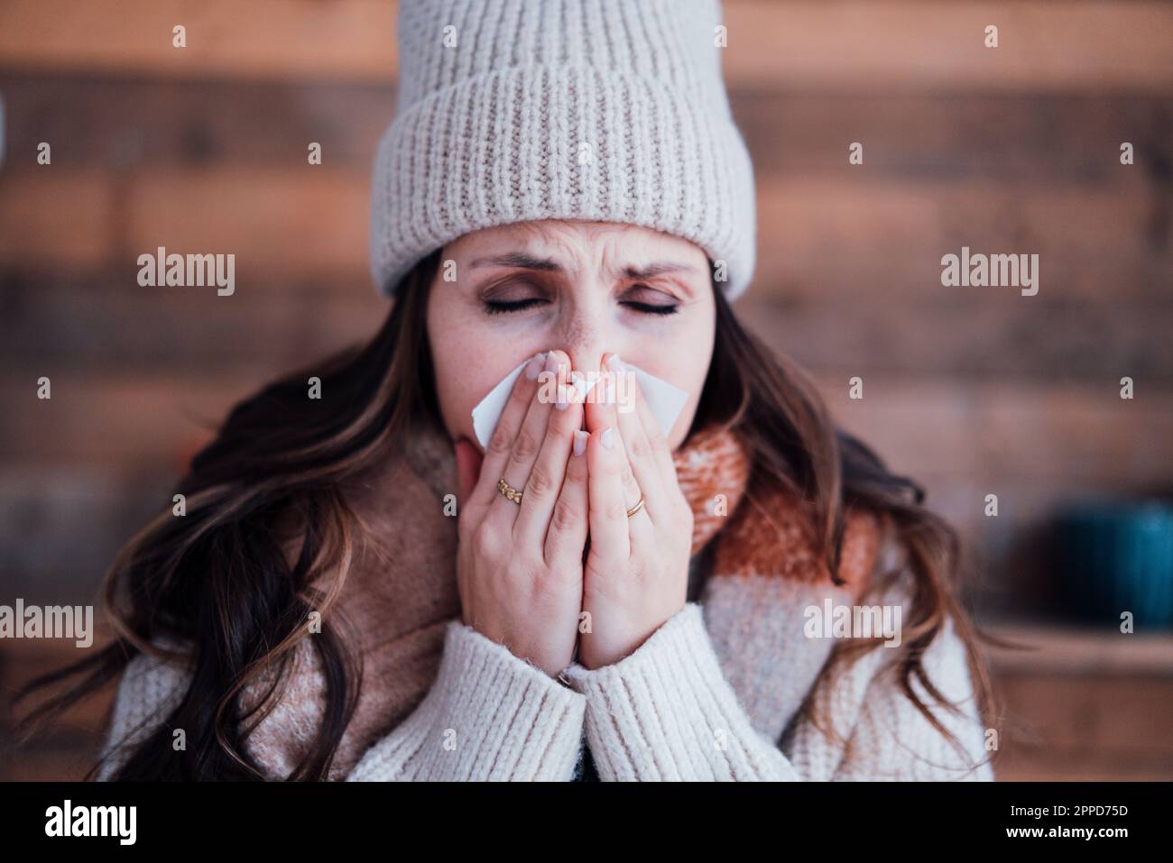 Sick woman wearing knit hat blowing nose Stock Photo - Alamy
