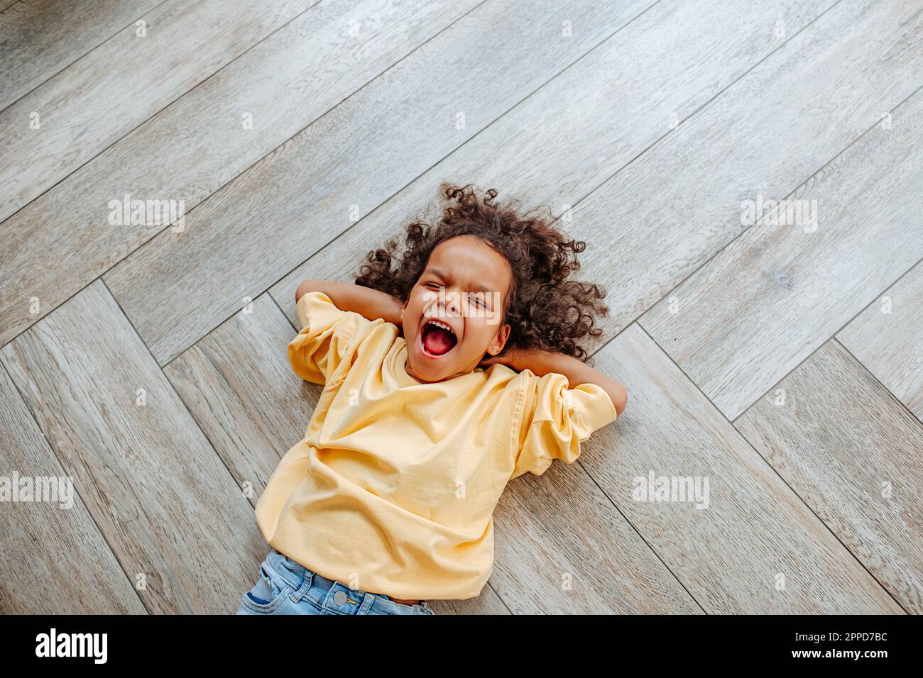 Cute girl yawning and lying on wooden floor at home Stock Photo - Alamy