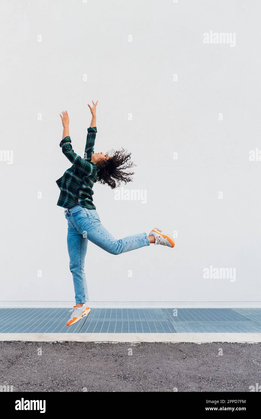 Young woman jumping in front of wall Stock Photo - Alamy