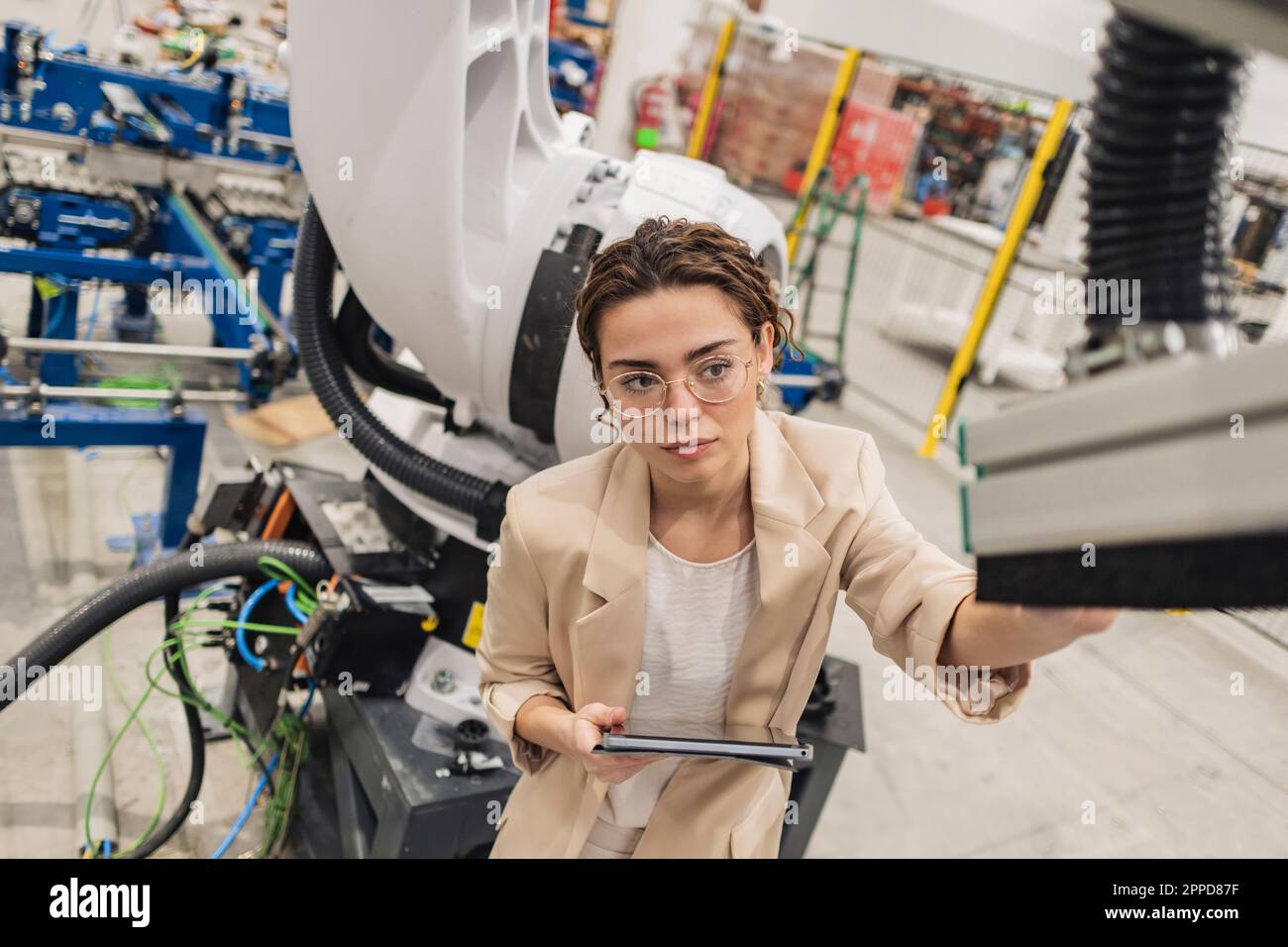 Young engineer wearing eyeglasses examining robotic arm in industry ...
