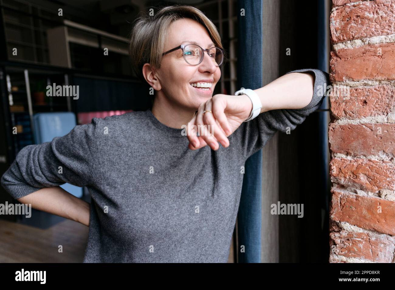 Happy mature woman talking through smart watch leaning on wall Stock ...