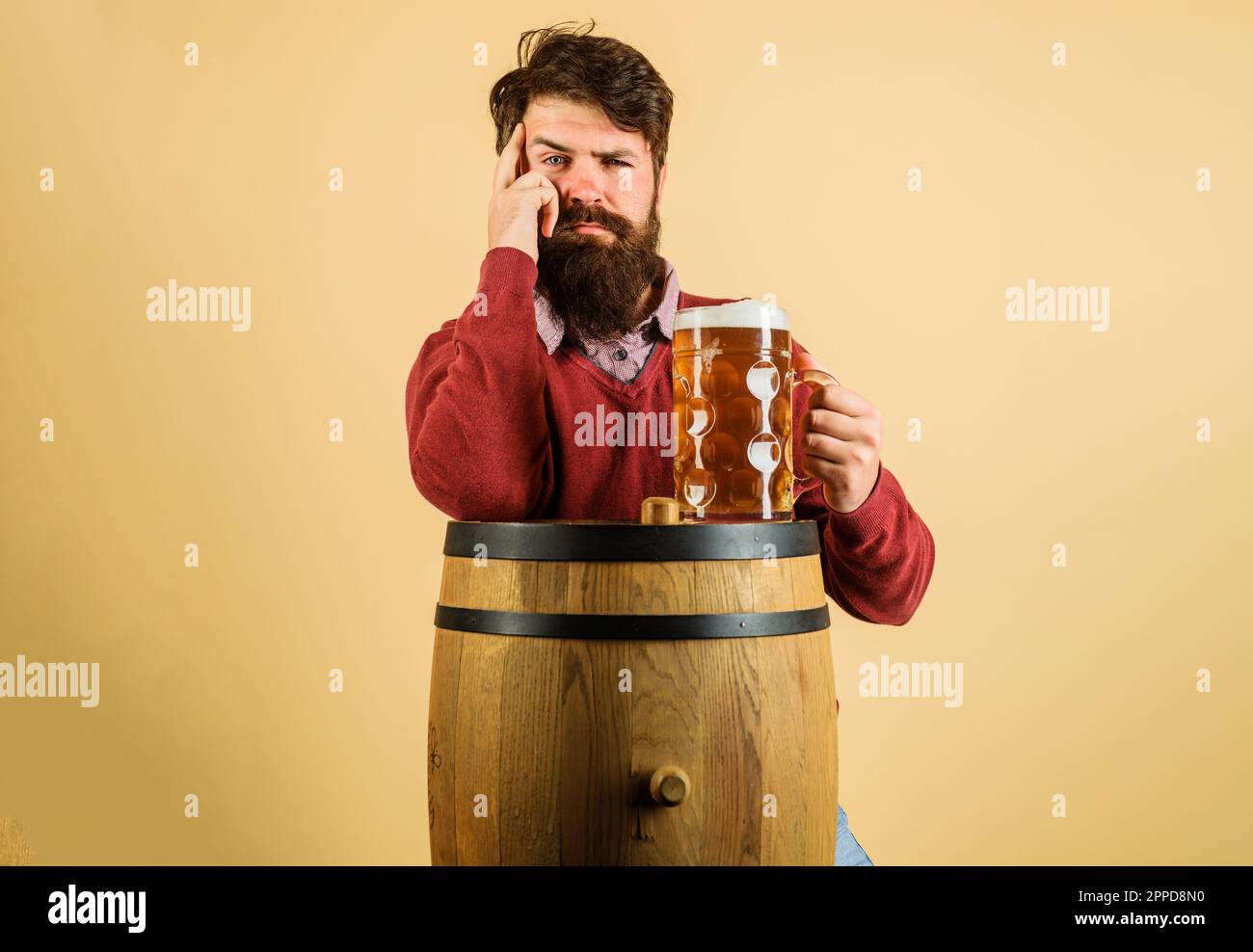 Beer time. Thoughtful brewer with mug of beer on wooden barrel. Serious ...