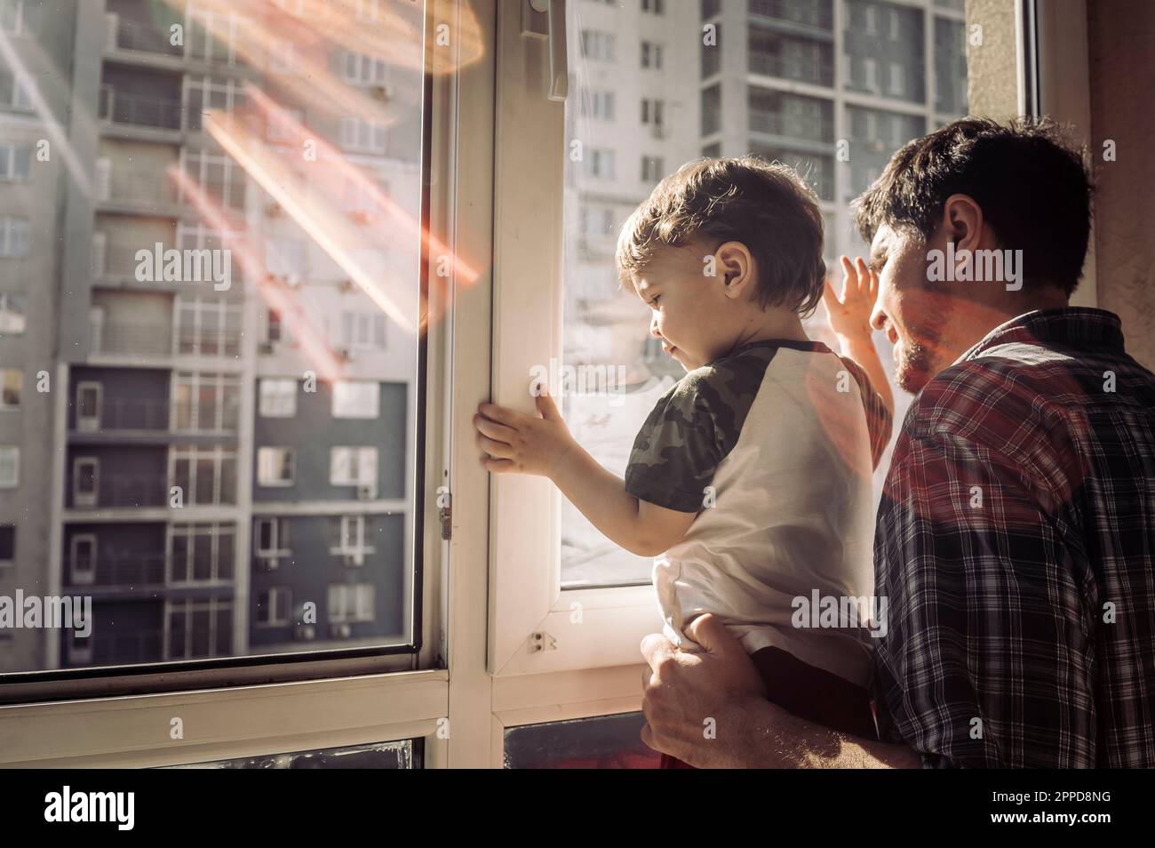 Father and son looking out of window at home Stock Photo - Alamy
