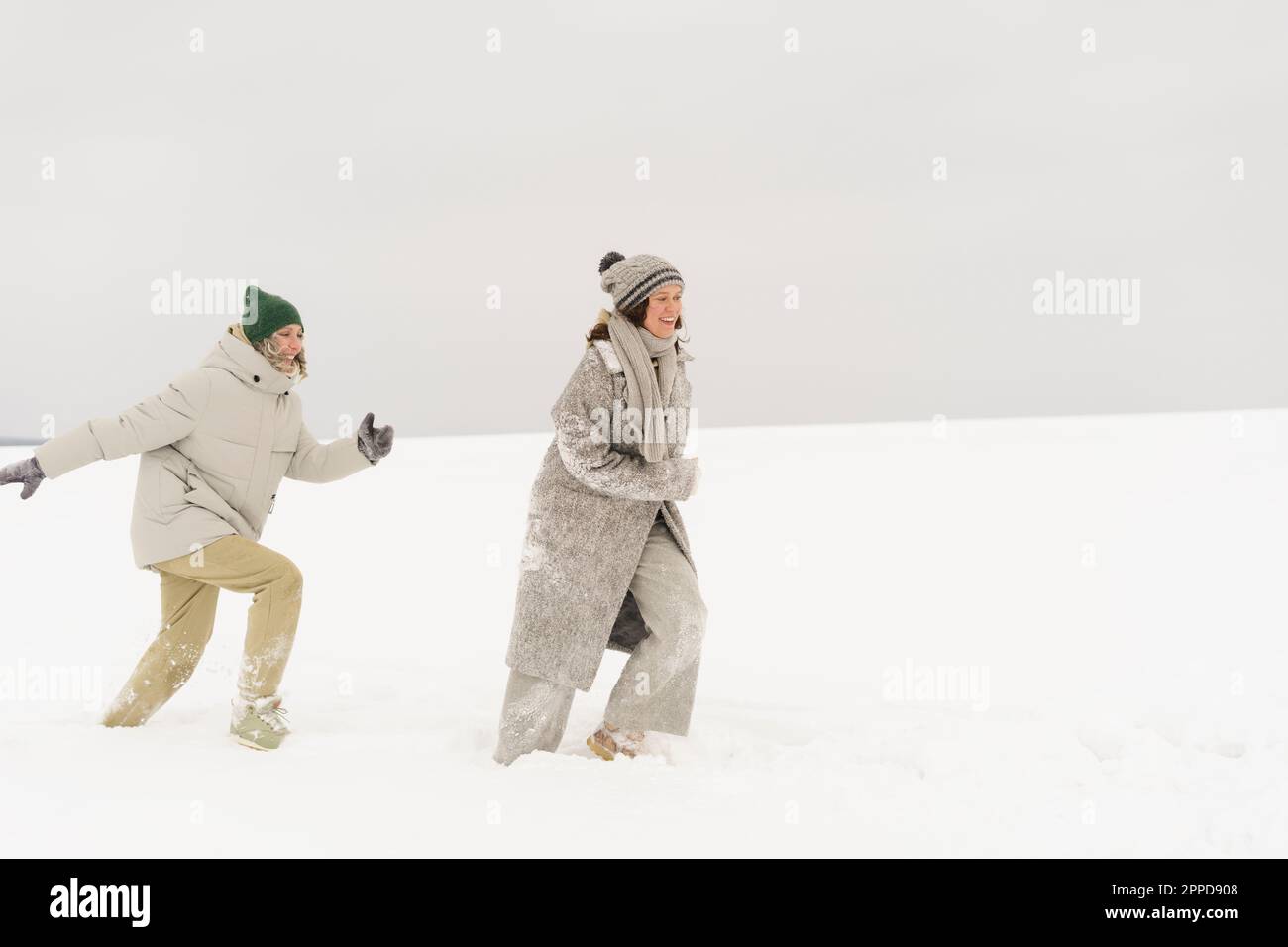 Happy woman running behind friend having fun in snow Stock Photo - Alamy