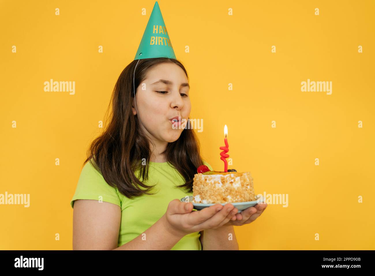 Girl blowing candle on birthday cake against yellow background Stock ...