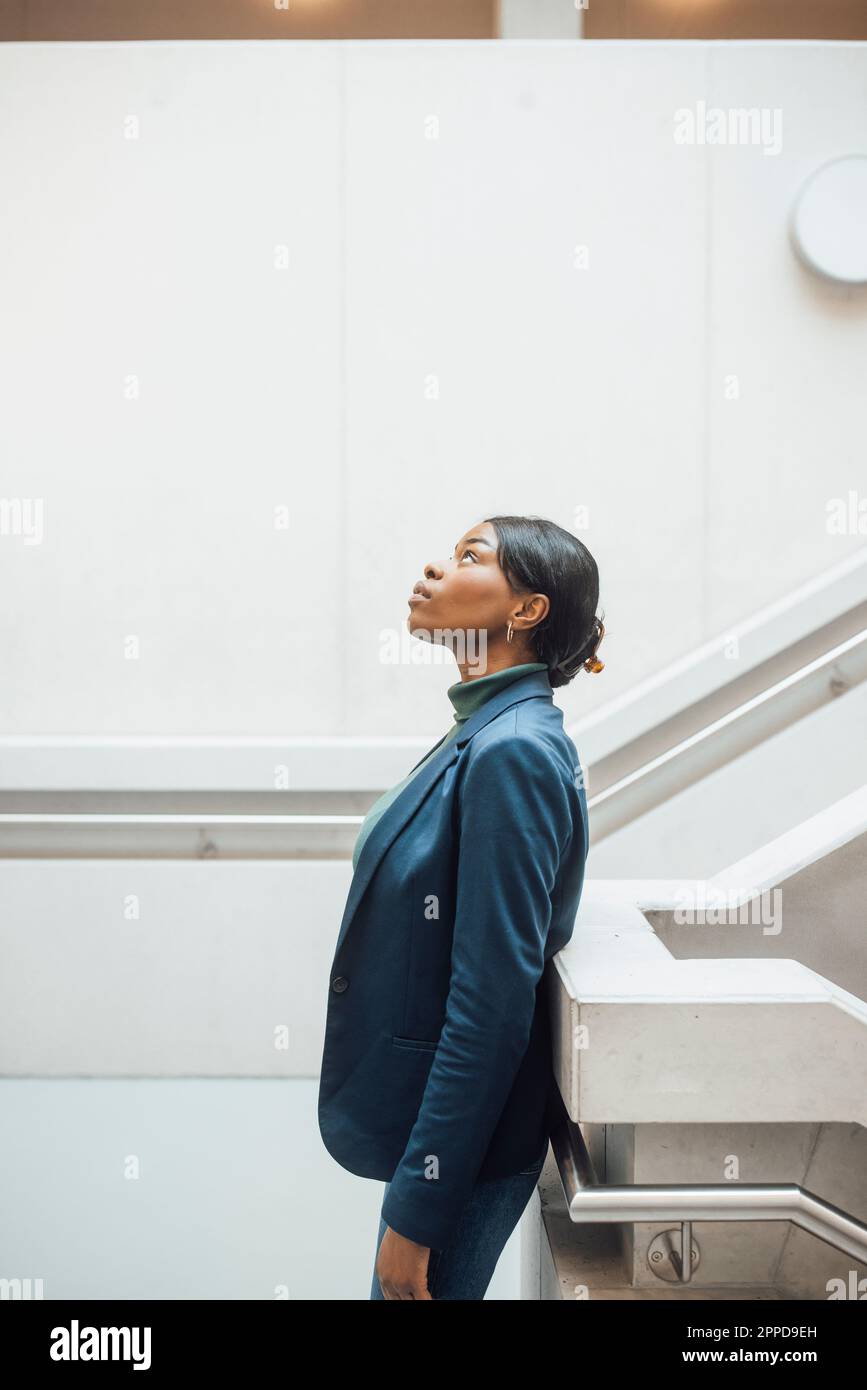 Businesswoman looking up standing near stairs railing Stock Photo - Alamy