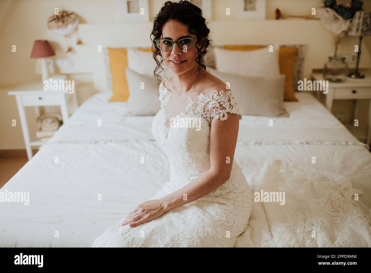 Smiling bride in wedding dress sitting on bed Stock Photo - Alamy