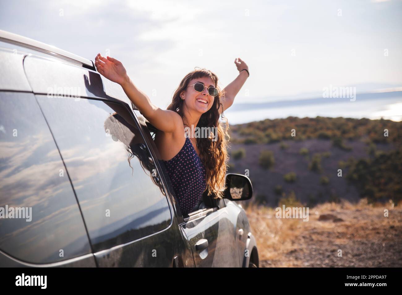 Happy young woman with arms raised leaning out of car window Stock ...