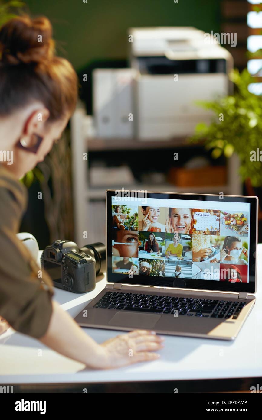 Seen from behind female photographer with laptop and photo camera ...