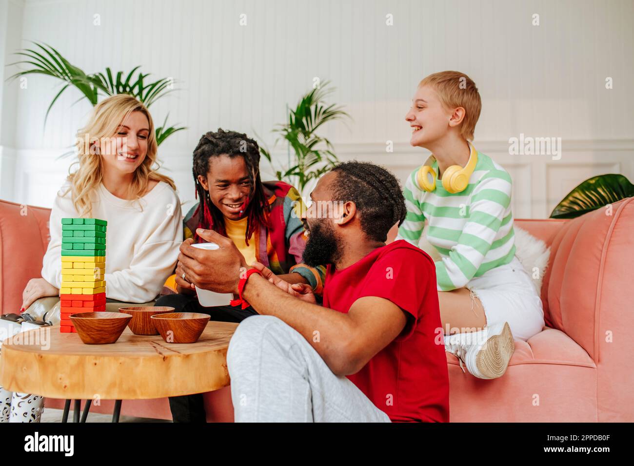 Young man sharing mobile phone with friends playing toy block game at ...