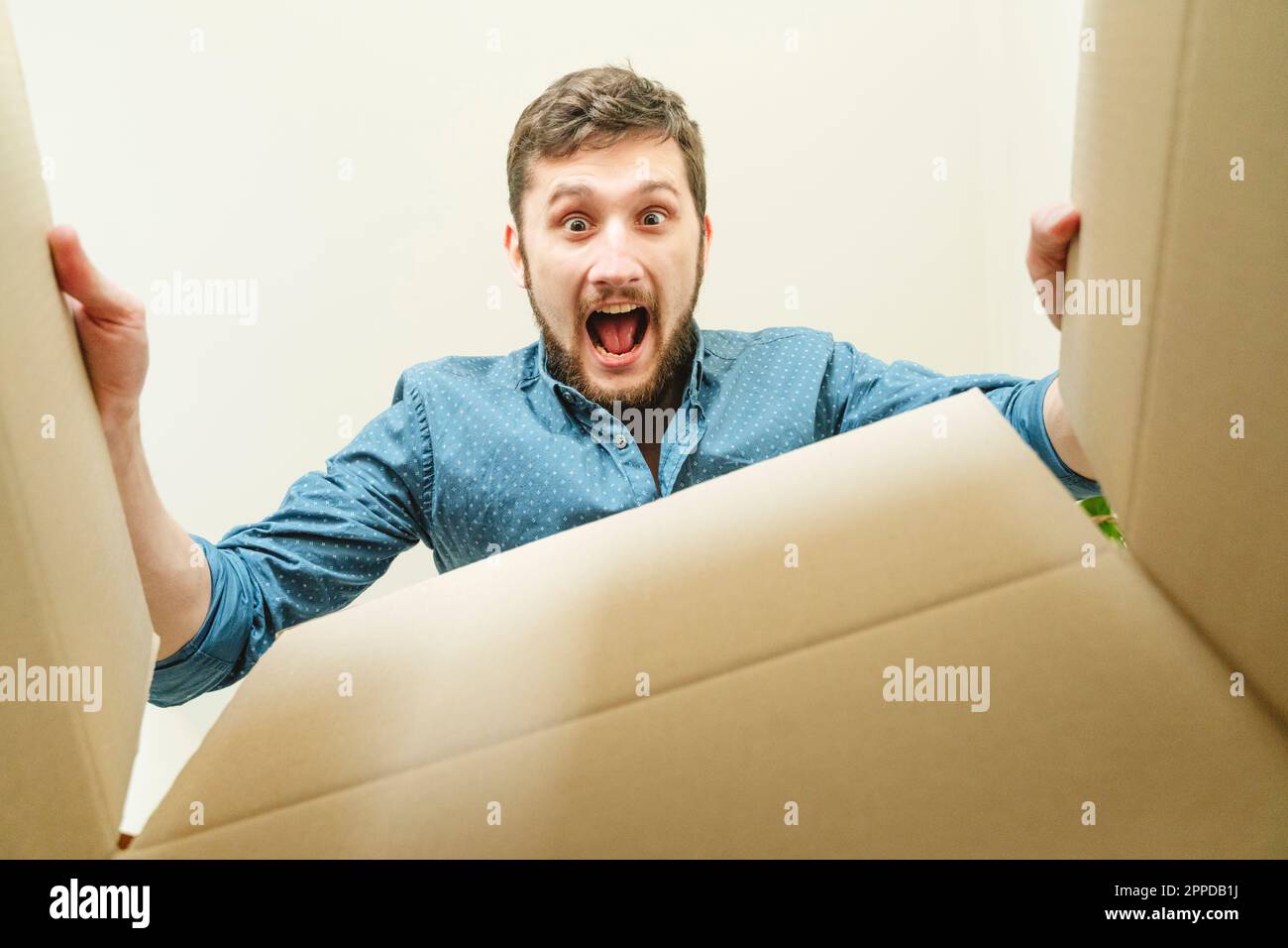Surprised young man looking into cardboard box in new home Stock Photo ...