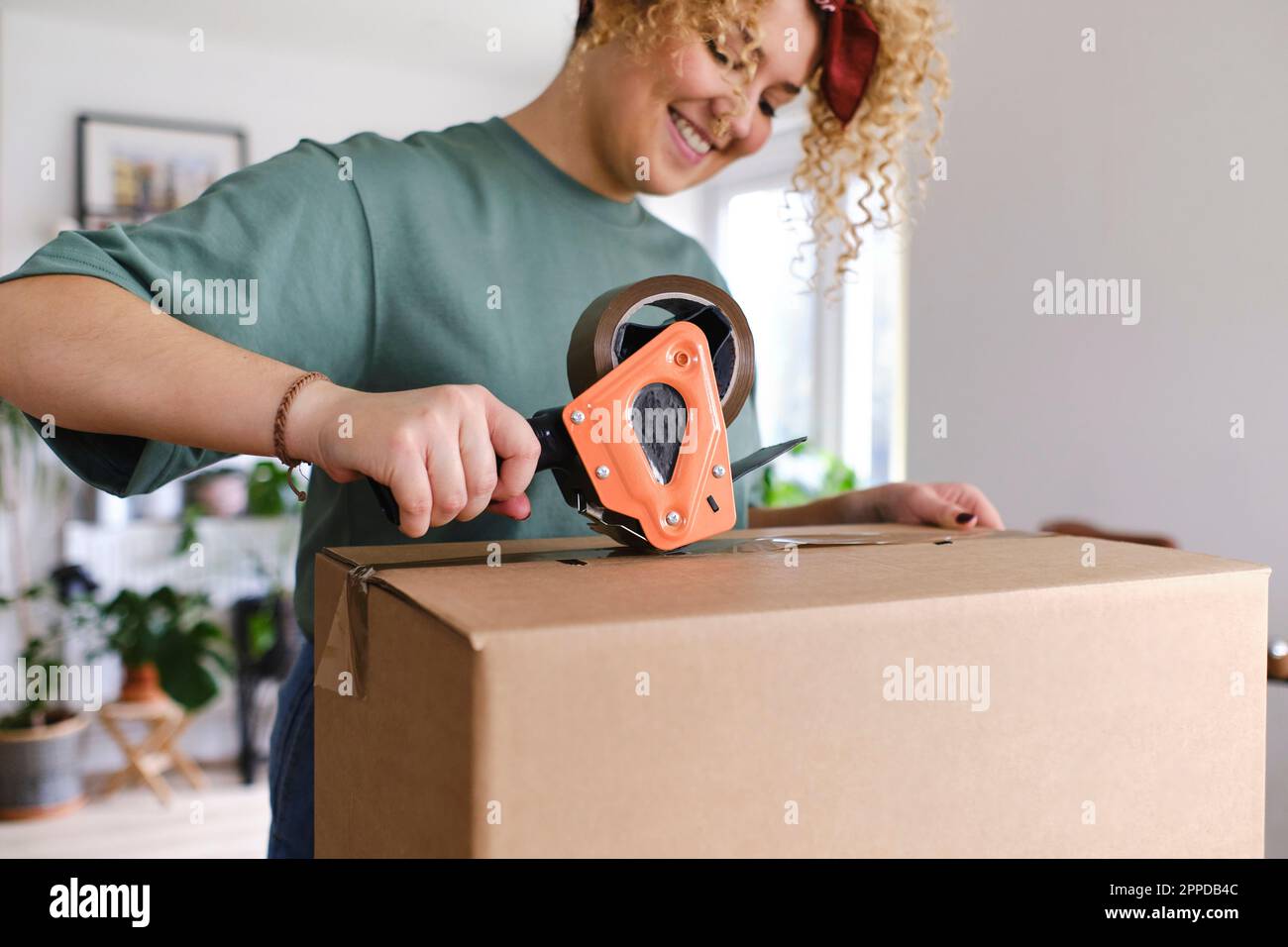 Smiling young woman packing box with adhesive tape Stock Photo - Alamy
