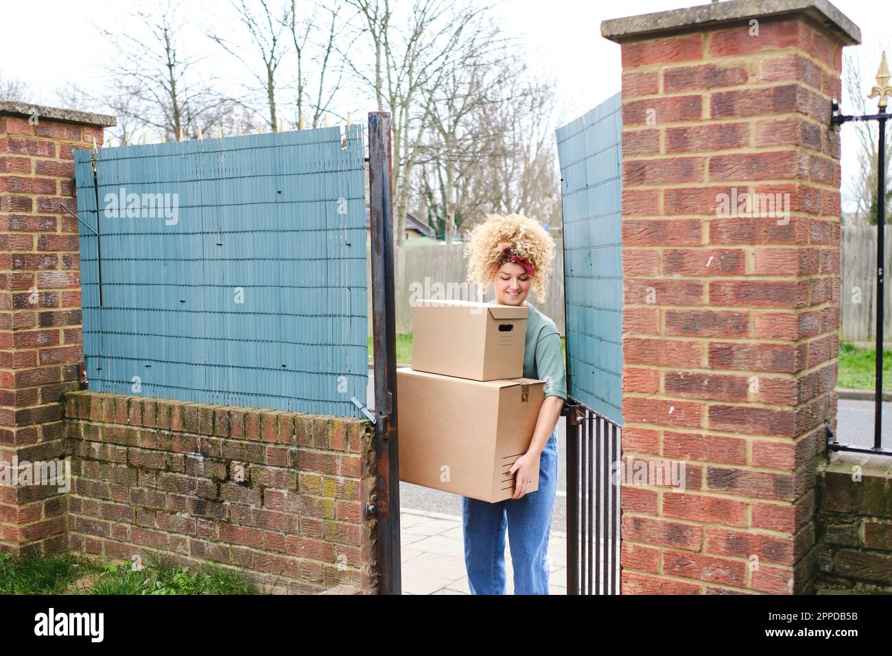 Happy woman delivering packages entering through gate Stock Photo - Alamy