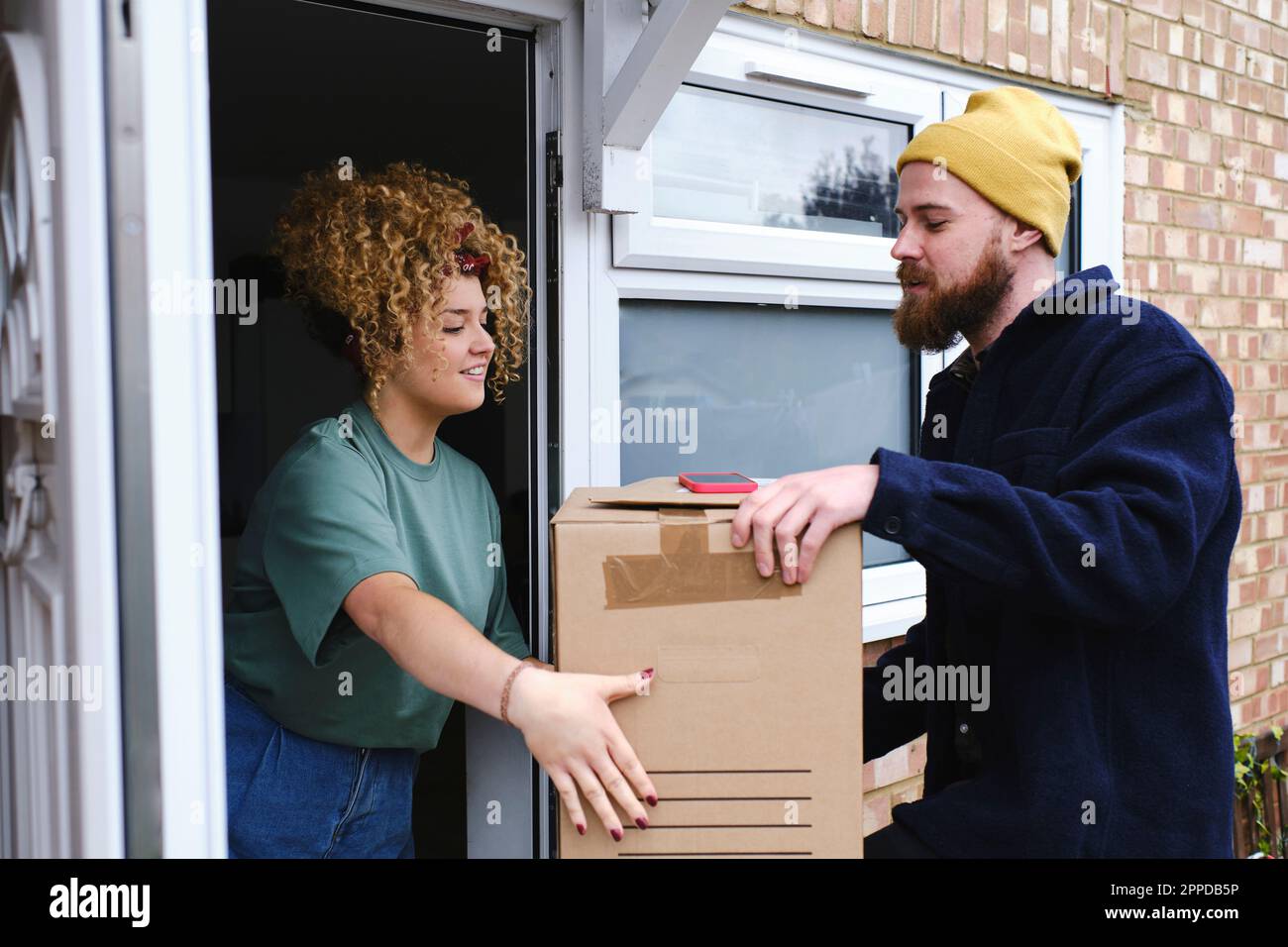 Happy young woman receiving boxes from delivery person Stock Photo - Alamy