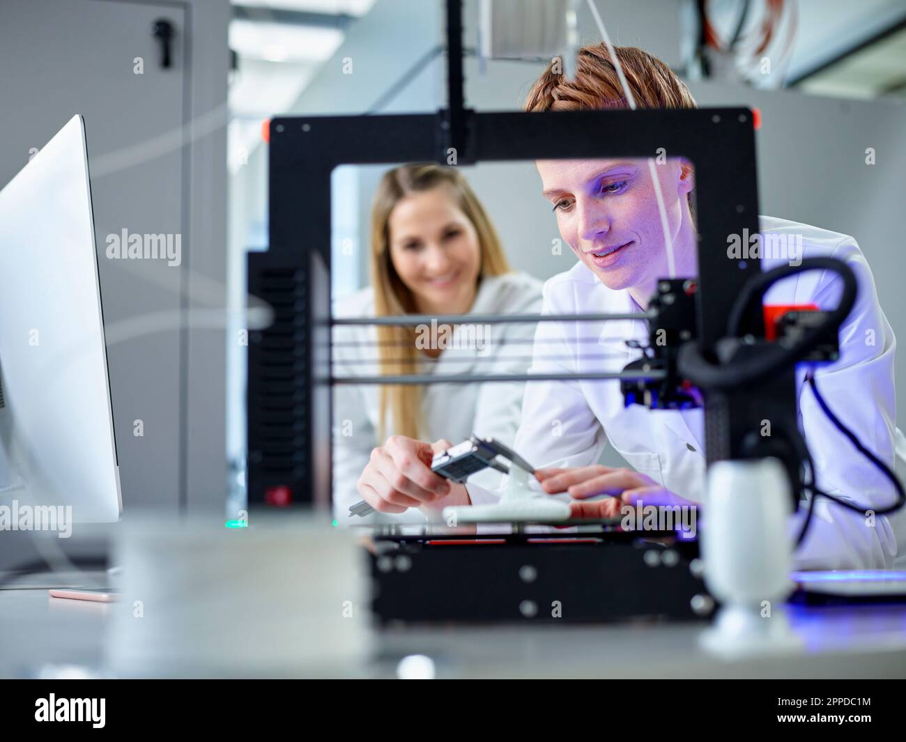 Engineer with colleague operating 3D printing machine in laboratory ...