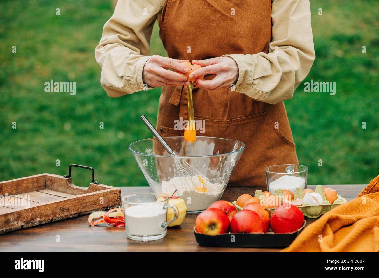 Woman breaking egg in mixing bowl at table in garden Stock Photo - Alamy