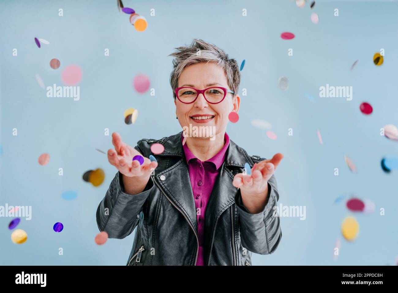 Happy mature woman wearing eyeglasses throwing confetti in front of ...