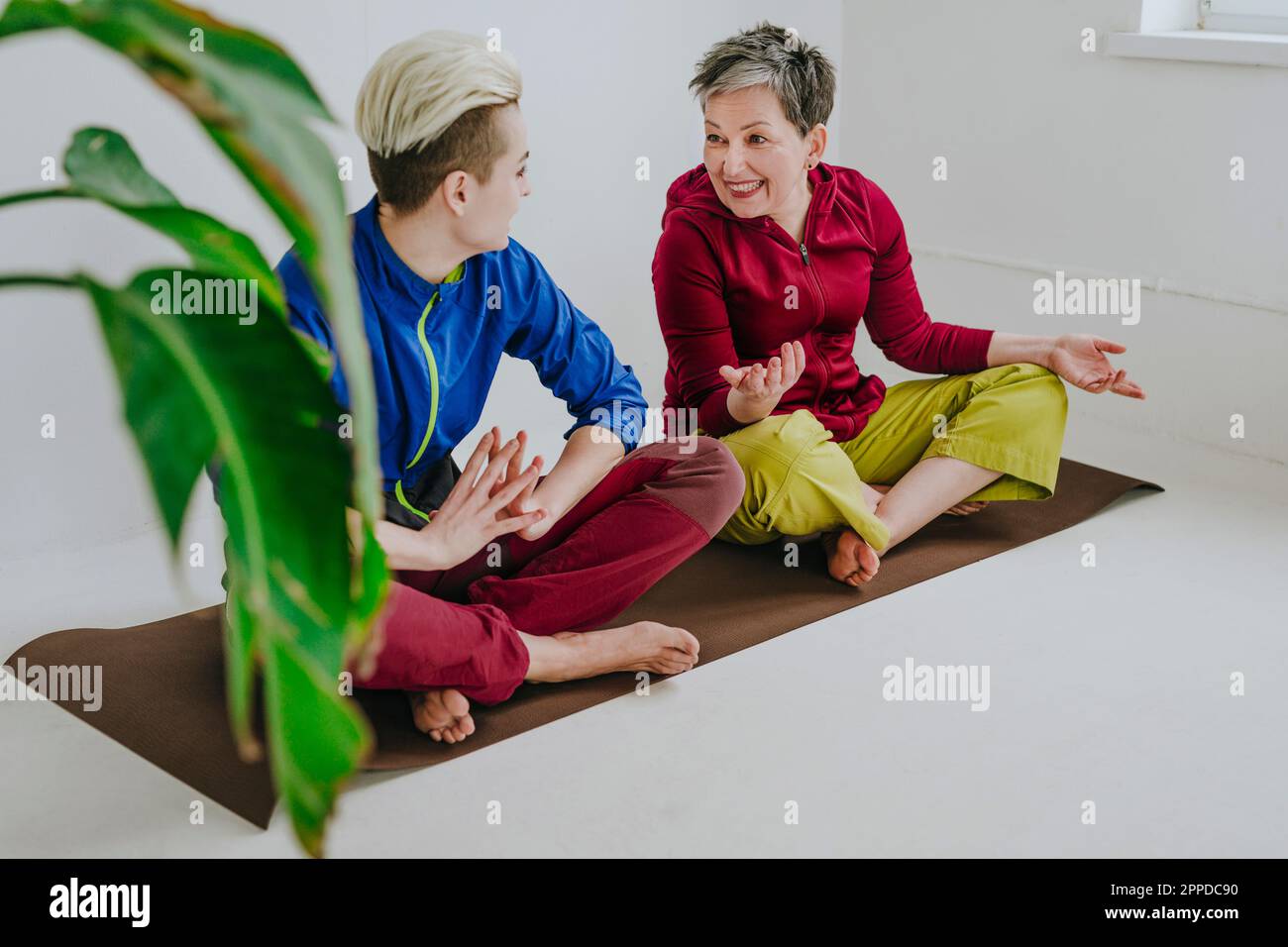 Happy mother talking to daughter sitting on exercise mat at fitness ...