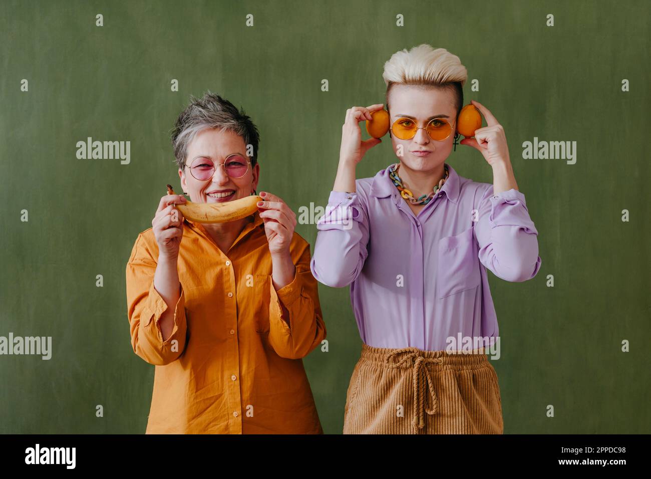 Happy women having fun with bananas and lemons in front of green wall ...