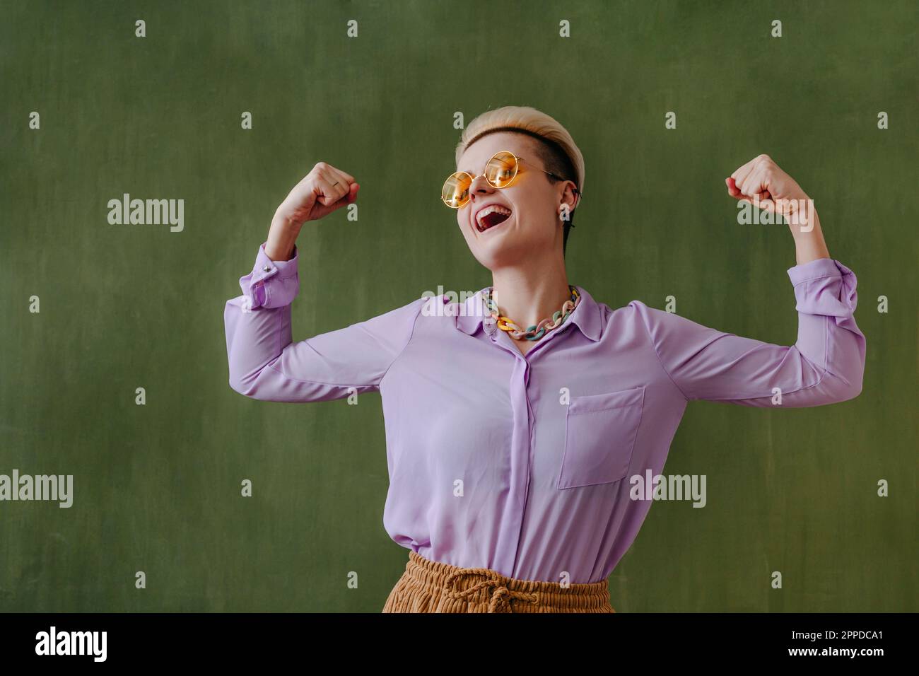 Happy young woman flexing muscles in front of green wall Stock Photo ...