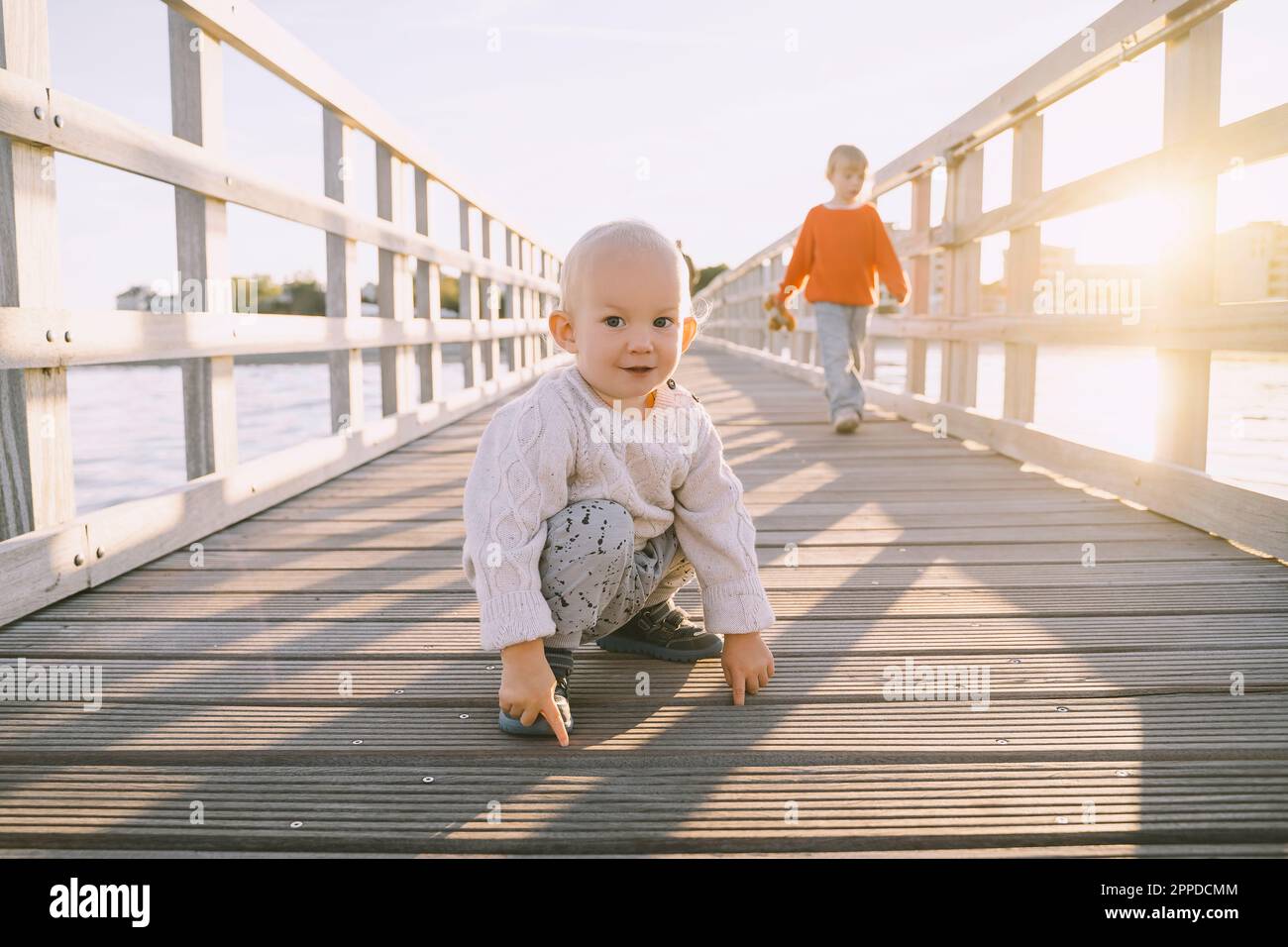 Cute boy crouching on wooden bridge with sister walking in background ...
