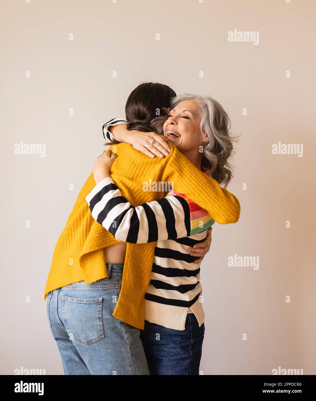 Smiling mature woman hugging daughter in front of wall Stock Photo - Alamy